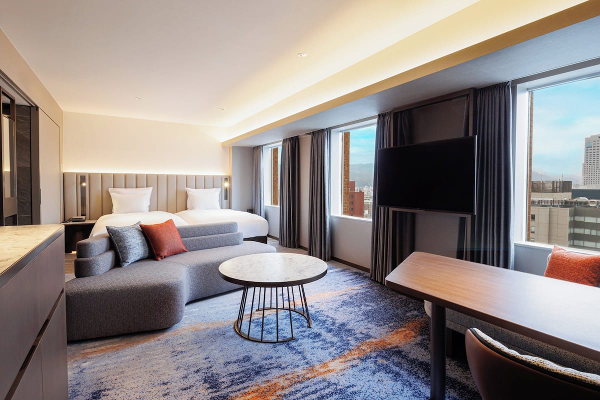 Quarto de hotel moderno com cama, sofá, mesa de jantar e televisão.
