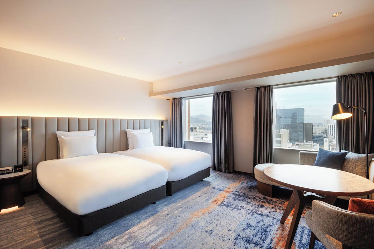 Quarto de hotel com uma cama grande, uma mesa pequena e vista para a cidade.