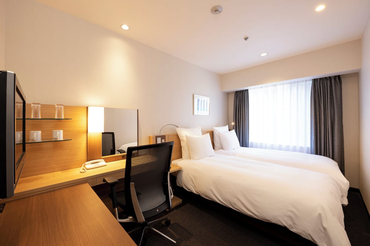 Quarto de hotel com cama, escrivaninha, cadeira e televisão.