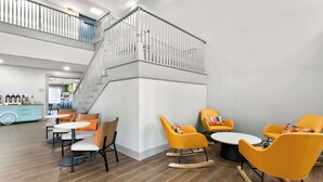 Um hall amplo com teto alto, escadaria e área de estar com cadeiras e mesas laranja.