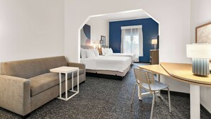 Quarto de hotel com sofá, mesa pequena, escrivaninha e cama.