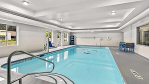 Uma piscina interior com pistas demarcadas, uma cadeira de salva-vidas e uma mesa à beira da piscina.