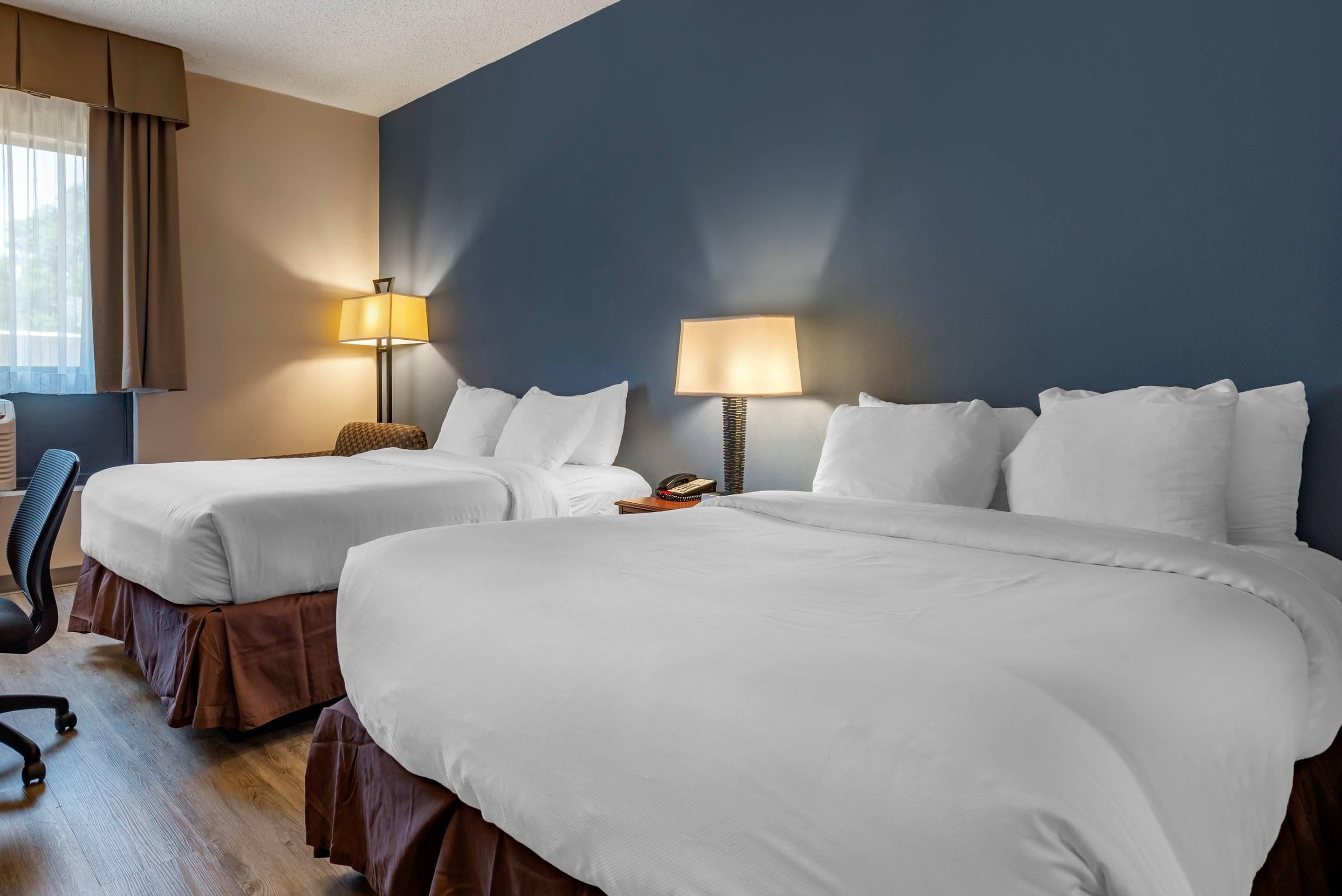 Quarto de hotel com duas camas, uma escrivaninha, uma cadeira e duas luminárias.