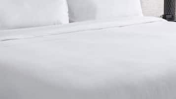Cama bem arrumada com roupa de cama branca e cabeceira escura.