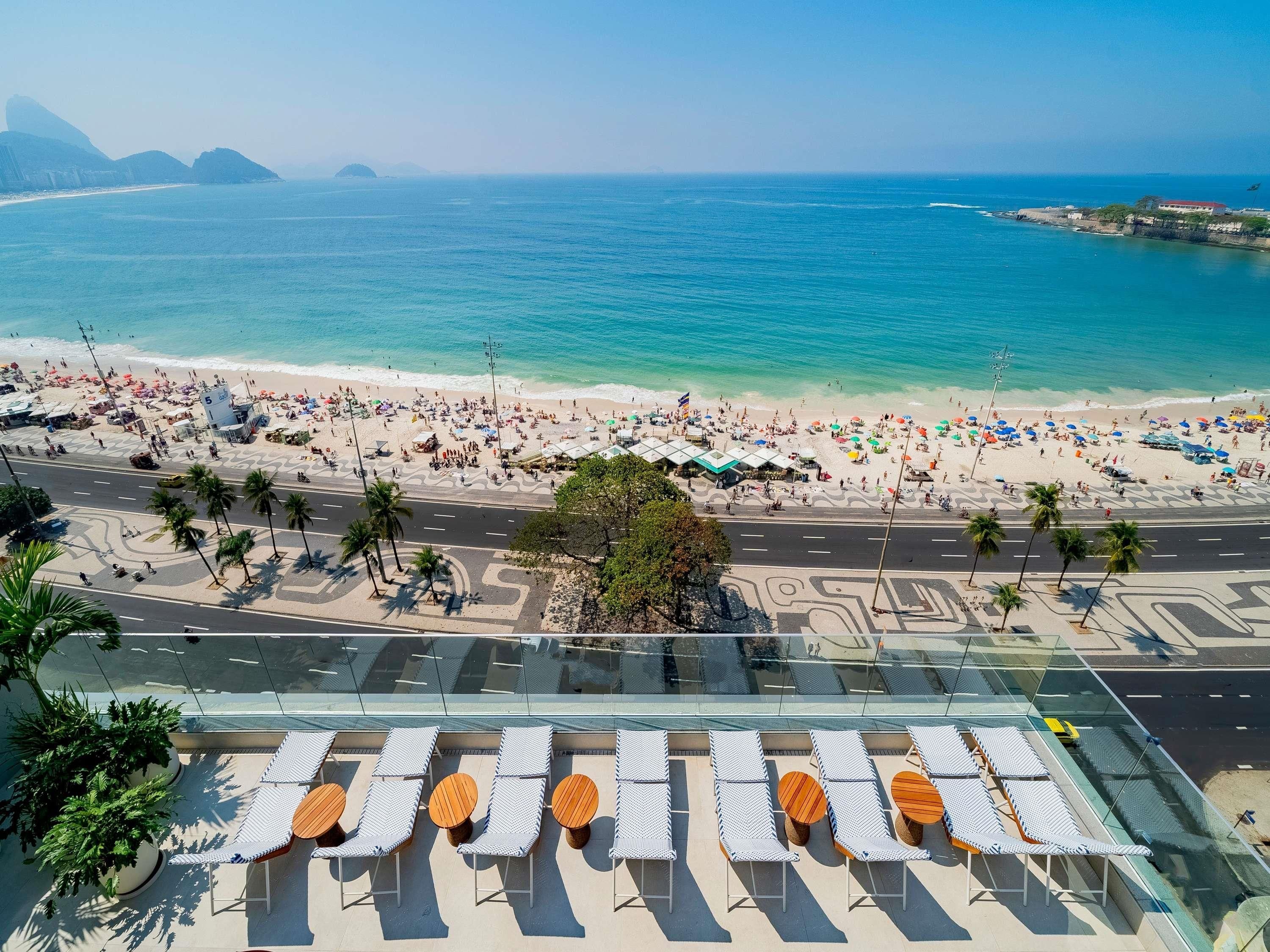 Um hotel à beira-mar com área de estar externa, vista para a praia e uma estrada ao primeiro plano.