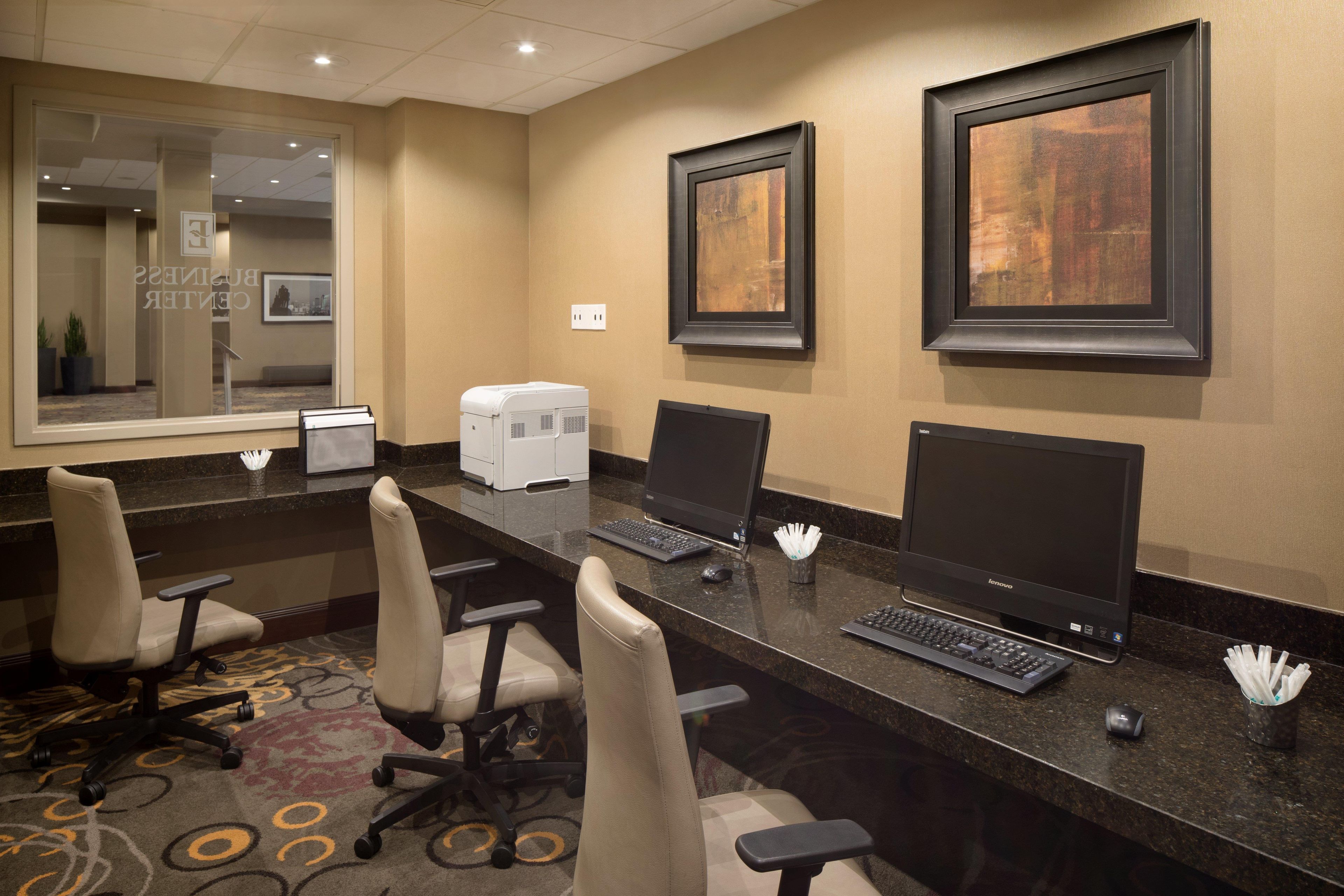 Uma área de recepção de hotel com um balcão comprido, vários computadores e quadros decorativos na parede.