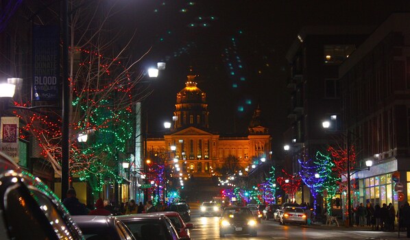 Rua arborizada decorada com luzes coloridas, um edifício com cúpula e carros na via.