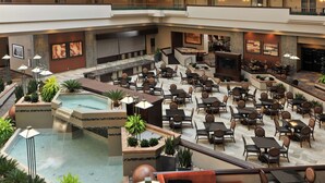 Um saguão de hotel com vários níveis, piscina central, área de refeições e bar.