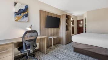 Quarto de hotel com cama, escrivaninha, cadeira, televisão, guarda-roupa e piso coberto por carpete.