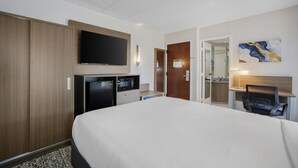 Quarto de hotel com uma cama grande, televisão na parede, escrivaninha com cadeira e micro-ondas.