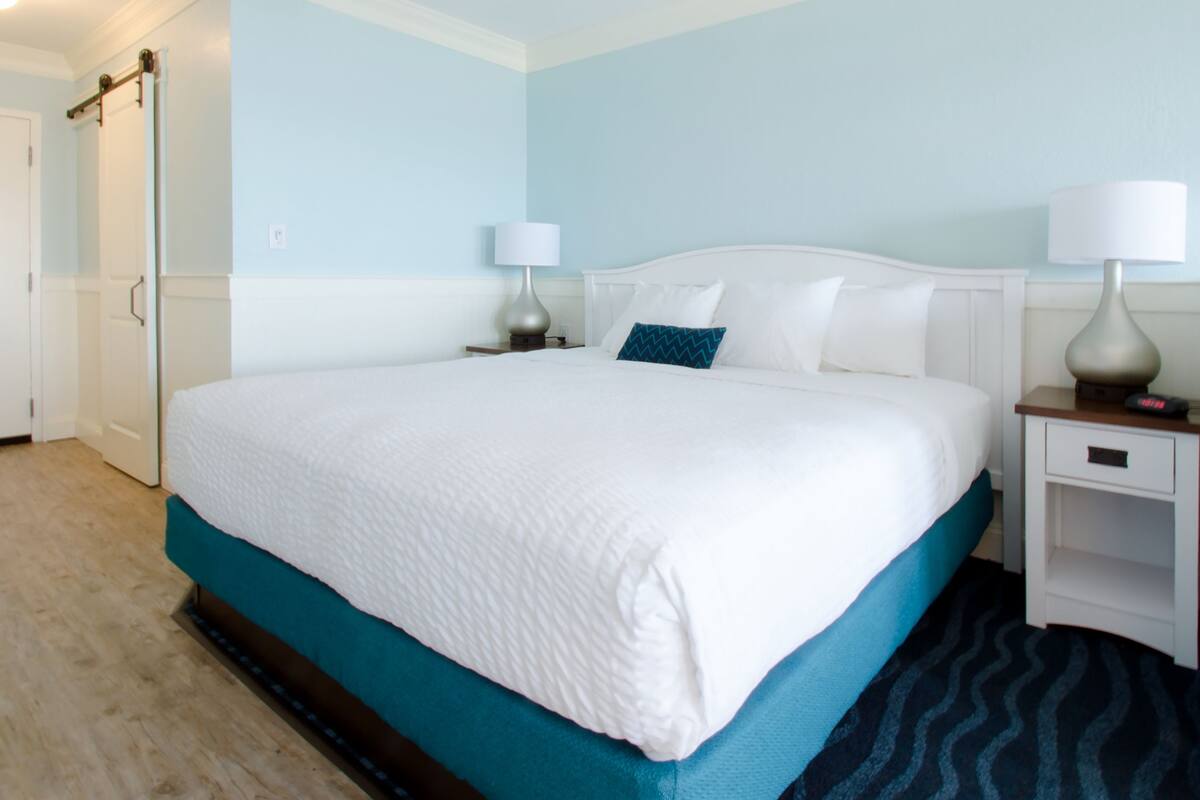 Quarto de hotel com uma cama grande, duas mesas de cabeceira com luminárias, um guarda-roupa e a porta do banheiro.