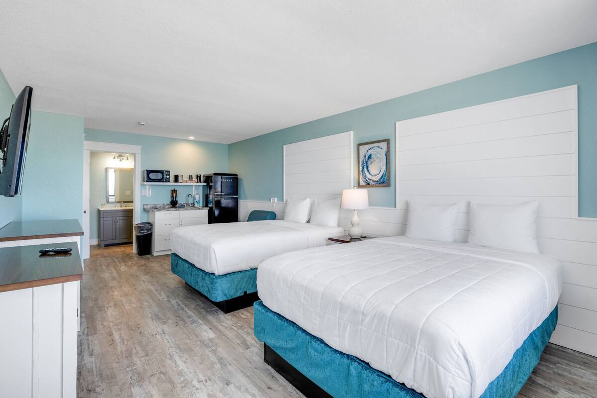 Quarto de hotel com duas camas, uma kitchenette e um banheiro.