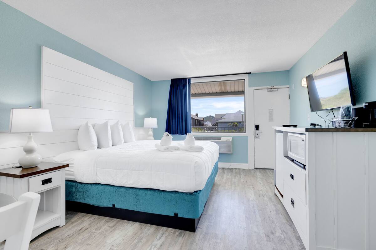 Quarto de hotel moderno com uma cama grande, uma escrivaninha, uma televisão e vista para a cidade.