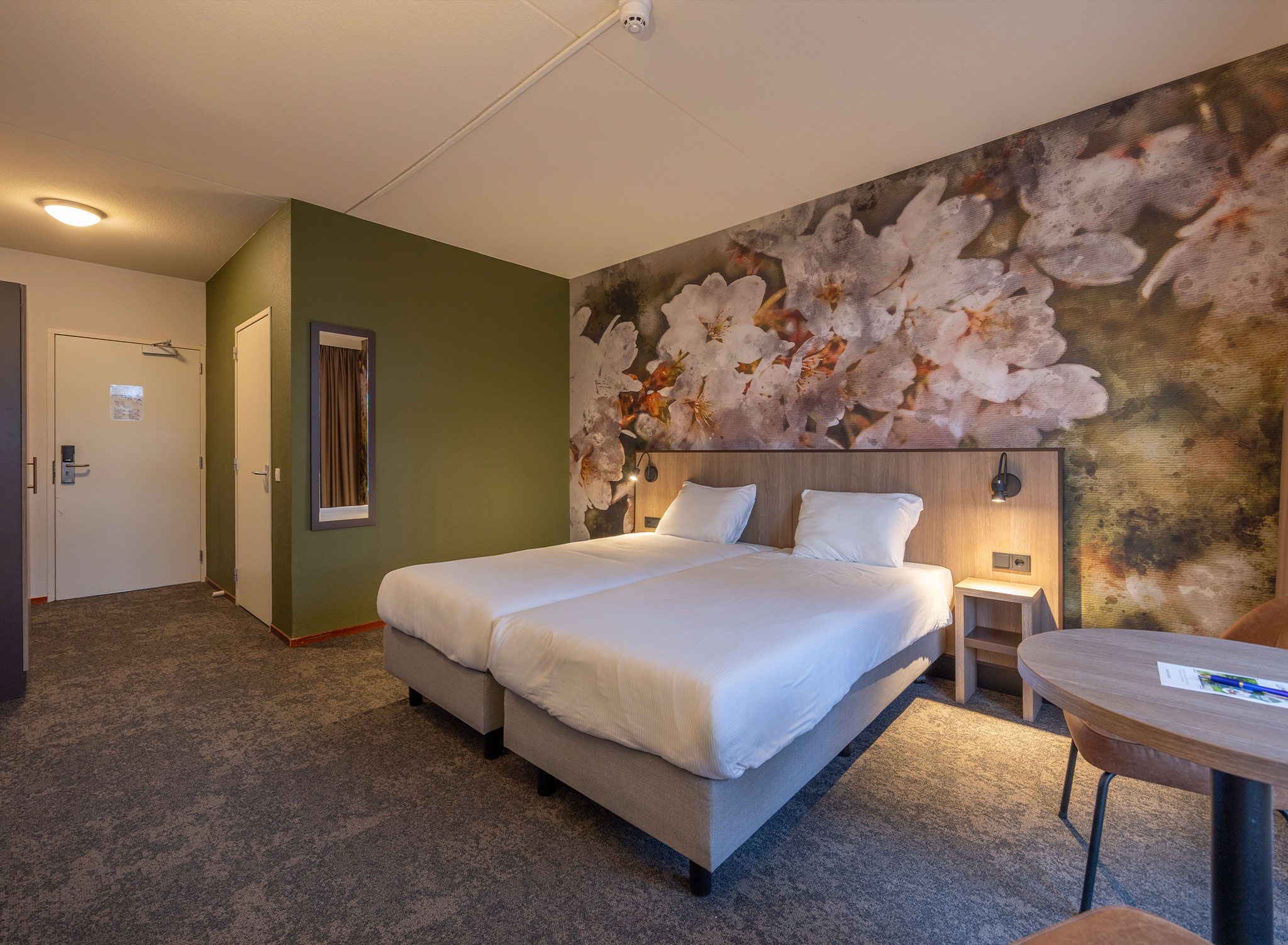 Quarto de hotel com uma cama grande, uma mesa pequena e uma parede com um quadro floral.