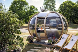 Estrutura esférica com uma mesa e cadeiras no interior, rodeada por um jardim com diversas plantas e flores.