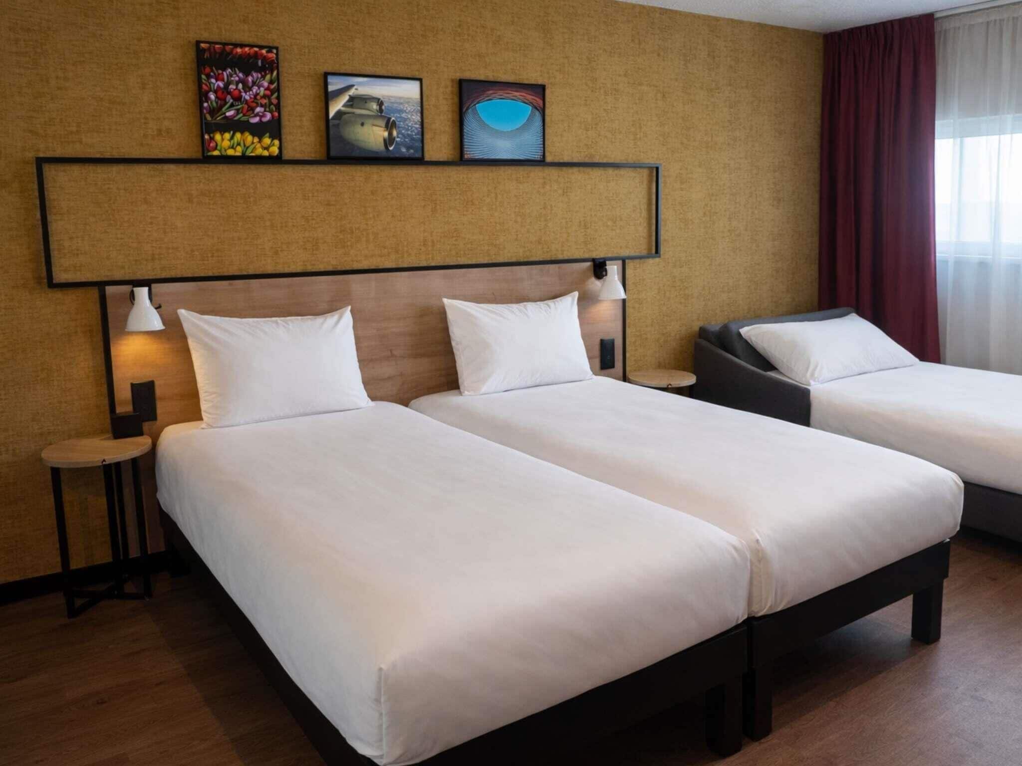 Quarto de hotel com duas camas, uma cabeceira grande e obras de arte na parede.