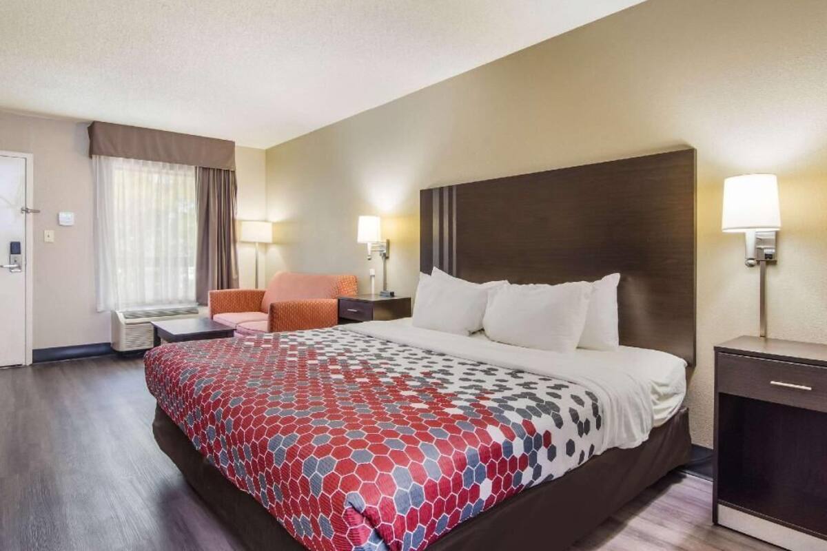 Quarto de hotel com uma cama grande, uma escrivaninha, uma cadeira e uma janela com cortinas.