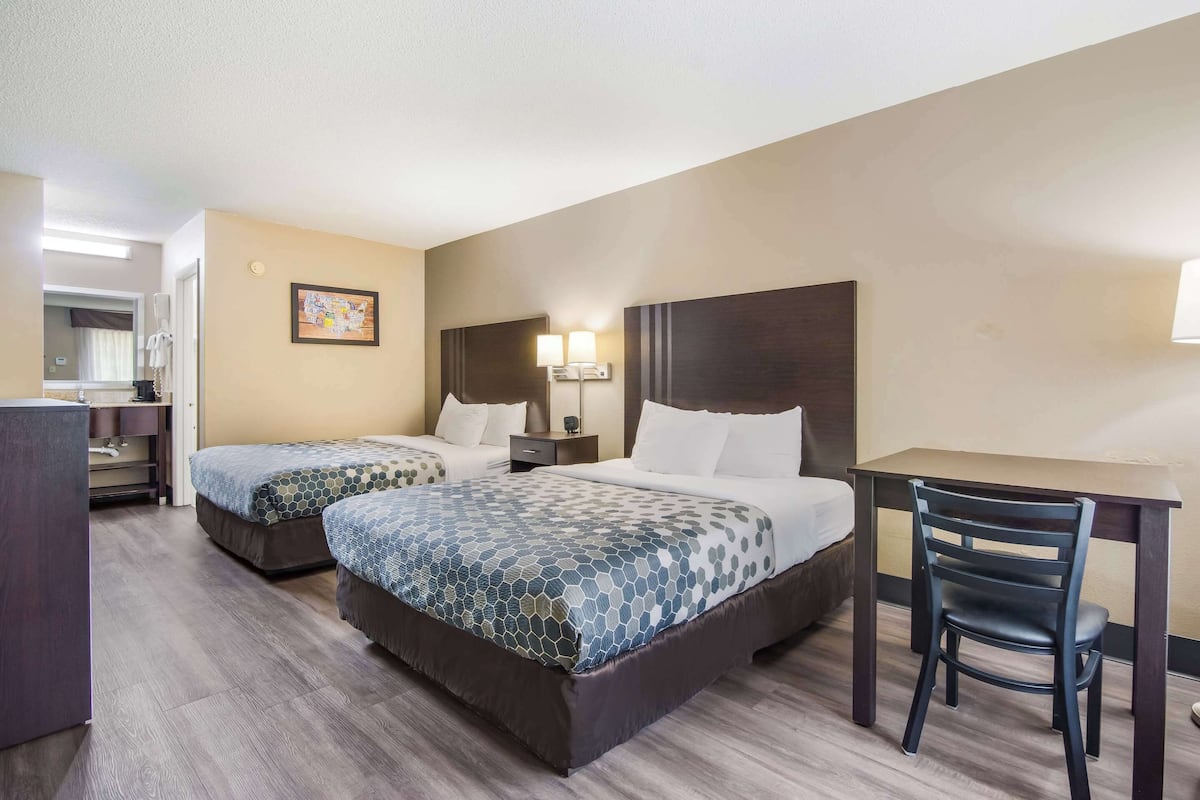 Quarto de hotel com duas camas, uma escrivaninha e uma cadeira.