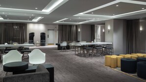 Uma sala de conferências moderna com uma mesa comprida, cadeiras pretas e brancas e um espaço de estar com pufes amarelos.
