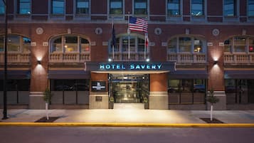 Entrada de hotel com uma placa indicando 'HOTEL SAVERY' e uma bandeira americana.