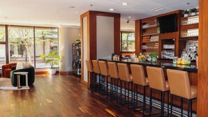 Uma área de bar moderna com um balcão comprido, vários banquinhos e uma variedade de garrafas e copos nas prateleiras.