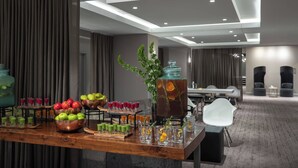 Um hall de hotel moderno com um balcão de recepção de madeira, uma grande taça para ponche e uma área de estar com cadeiras e mesas.