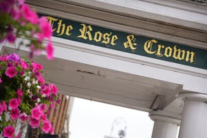 Um letreiro com o texto 'The Rose & Crown' na fachada de um edifício.