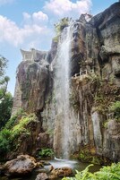 Uma cascata desce uma falésia rochosa, com um edifício tradicional no topo.