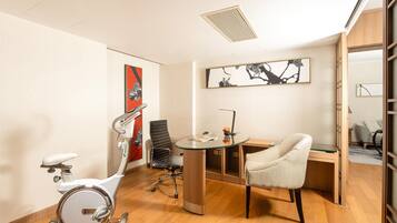 Quarto com bicicleta ergométrica, escrivaninha, cadeira e obras de arte nas paredes.