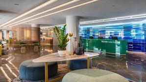 Um lobby moderno com balcão de recepção, áreas de estar e uma grande peça central de plantas.