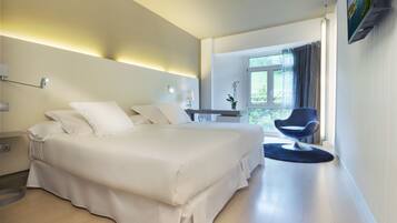 Quarto de hotel moderno com uma cama grande, uma cadeira, uma mesa e uma janela com cortinas.