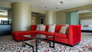 Um sofá modular vermelho com uma mesa de centro de vidro, tapete estampado e uma porta que dá para outro cômodo.