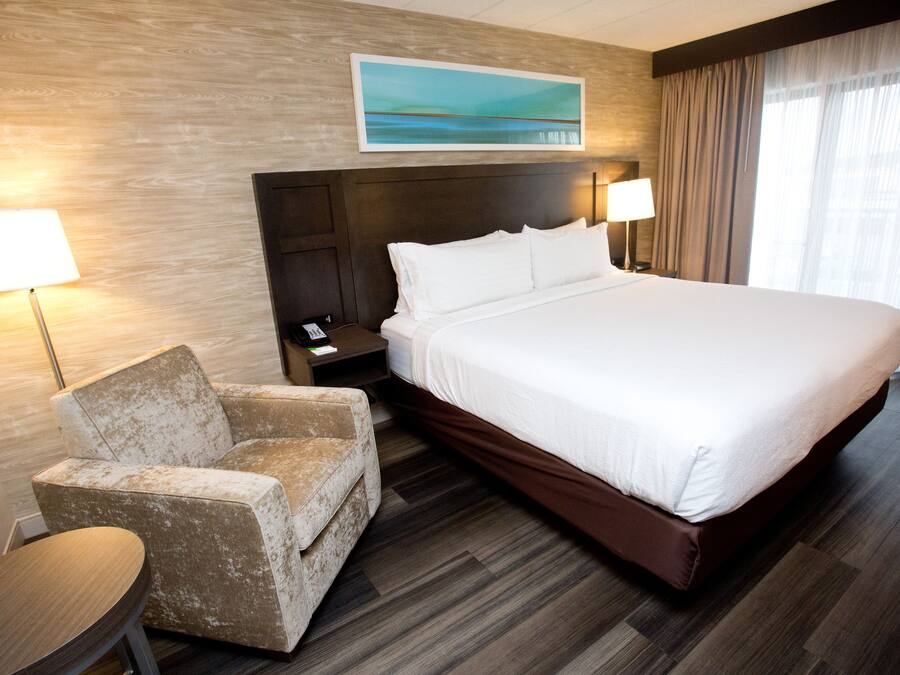 Quarto de hotel com uma cama grande, uma cadeira, uma mesa de cabeceira e um quadro na parede.