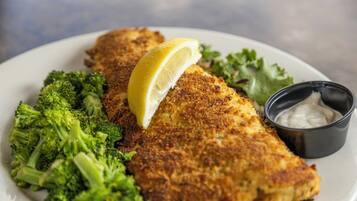 Um prato com escalope à milanesa, um pedaço de limão, brócolis e uma pequena tigela de molho.