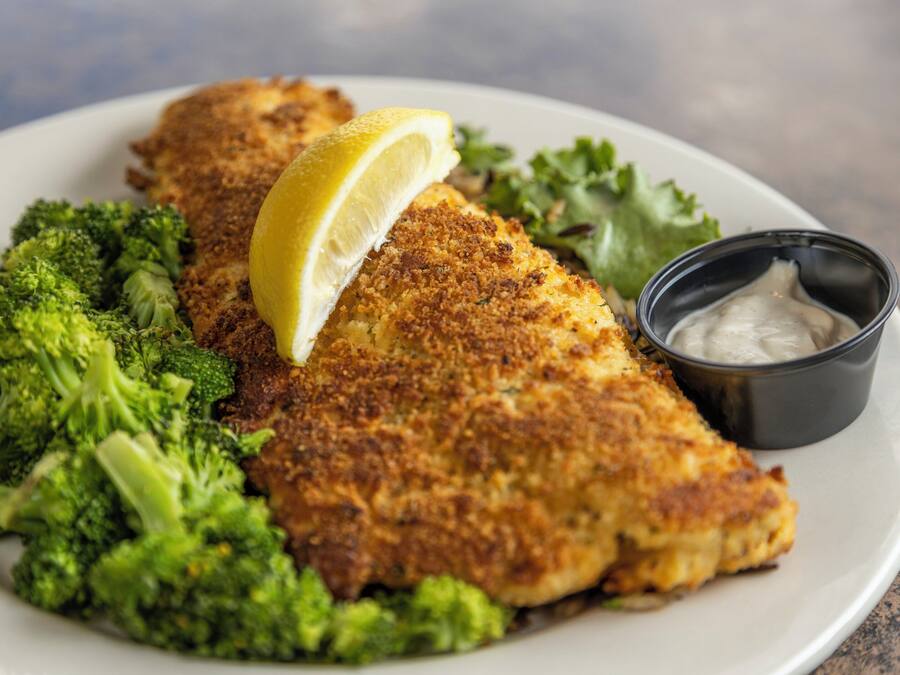 Um prato com escalope à milanesa, um pedaço de limão, brócolis e uma pequena tigela de molho.