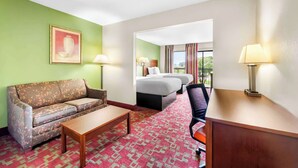 Quarto de hotel com sofá, secretária, cadeira, cama e janela com cortinas.