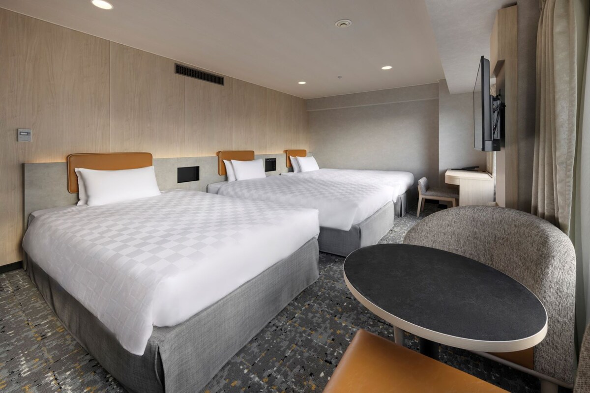 Quarto de hotel com duas camas, uma escrivaninha, uma cadeira e uma televisão.