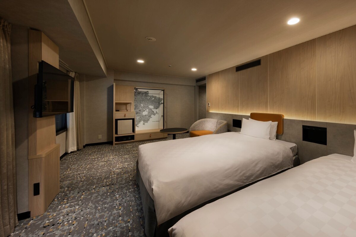 Quarto de hotel com duas camas, uma televisão de tela plana, um mapa na parede e uma pequena mesa com uma cadeira.