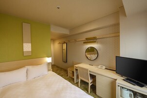 Quarto de hotel com cama, escrivaninha, cadeira, televisão e espelho.