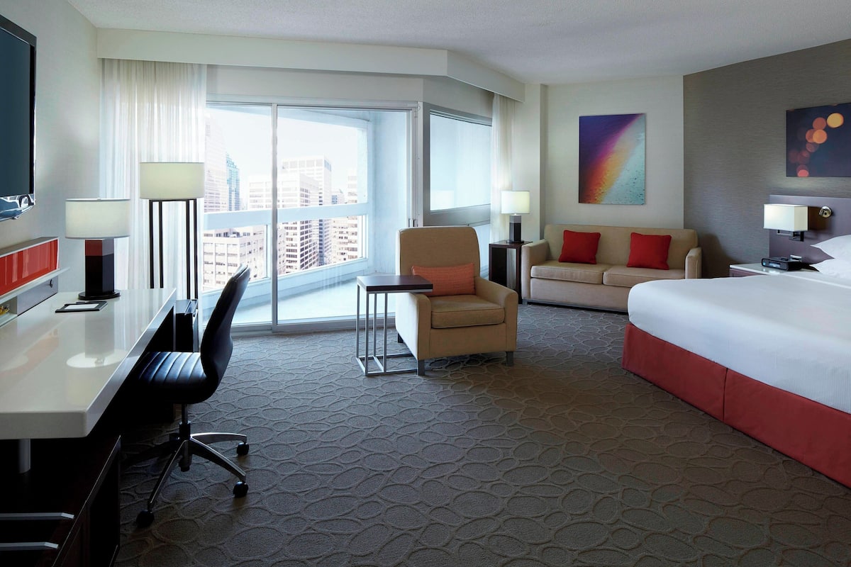 Quarto de hotel com cama, escrivaninha, cadeira, sofá e mesinha.
