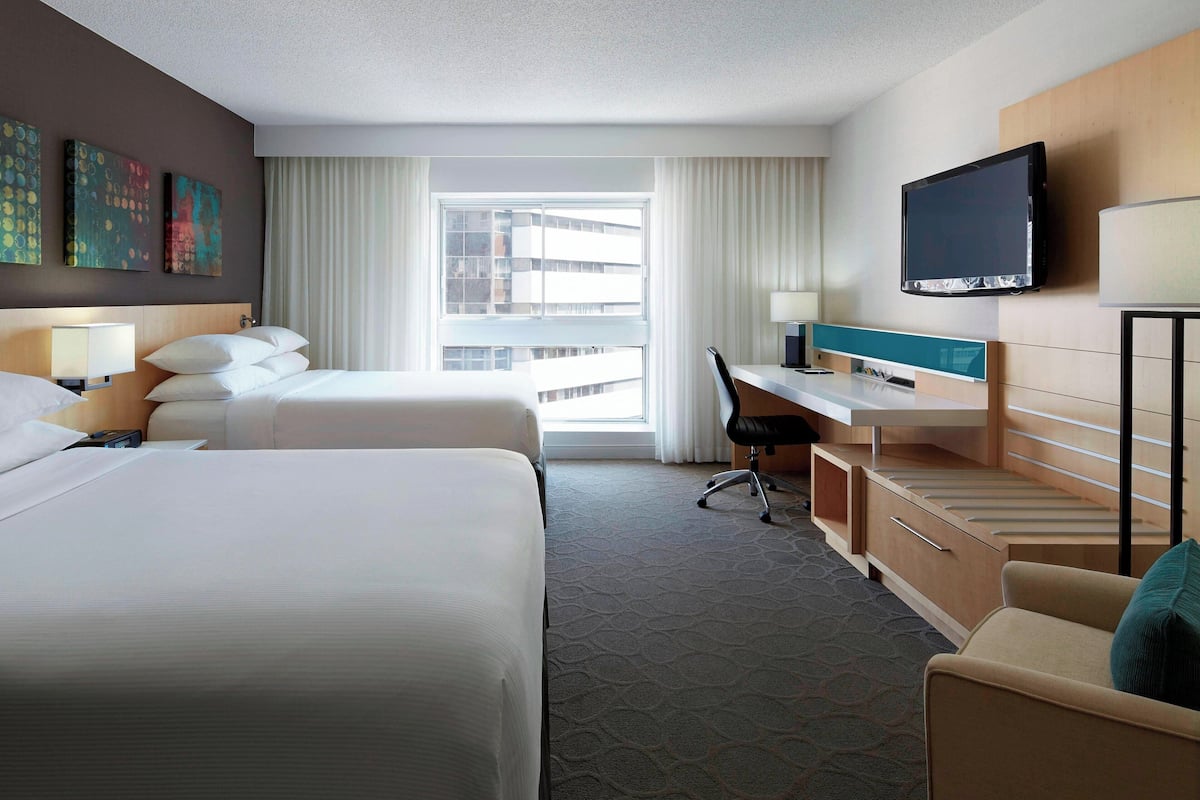 Quarto de hotel com duas camas, uma escrivaninha, uma televisão e vista para a cidade.