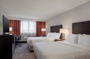 Quarto de hotel com duas camas, uma escrivaninha com televisão, uma cadeira e duas luminárias de cabeceira.