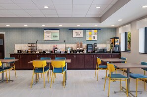 Cozinha moderna com estação de café, área de estar com mesas e cadeiras, e vista para o exterior.