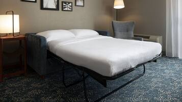 Quarto de hotel com cama, escrivaninha, cadeira, luminária e quadros na parede.