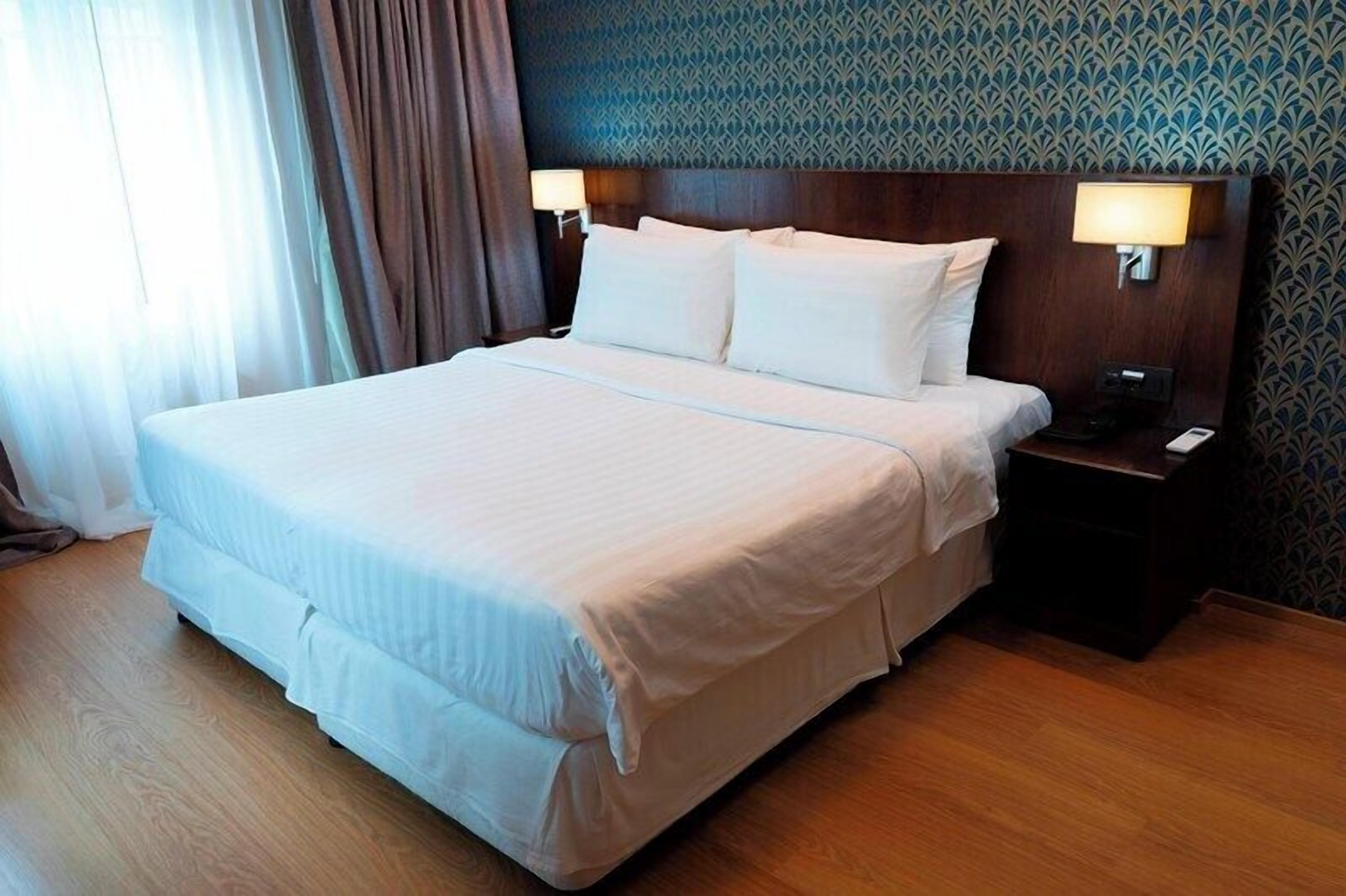 Quarto de hotel com uma cama grande, duas mesas de cabeceira com abajures e um papel de parede estampado.