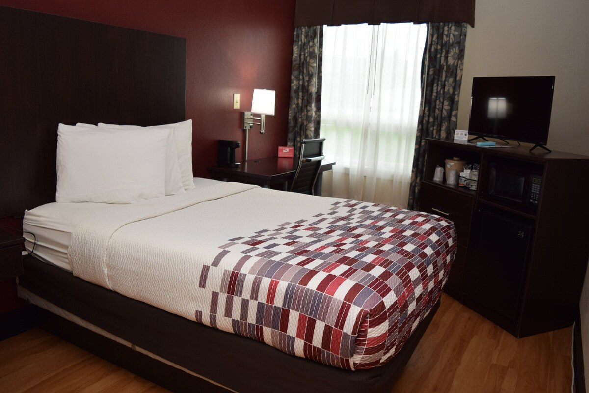 Quarto de hotel com cama grande, escrivaninha, televisão e armário.