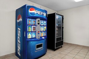 Uma máquina de Pepsi azul com diversas opções de bebidas e uma geladeira preta ao lado.