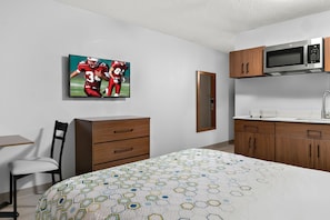 Quarto com cama, poltrona, cômoda, micro-ondas e um quadro na parede.