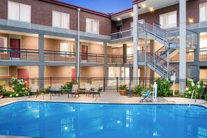 Um hotel com vários andares, piscina, área de estar externa e escadaria ligando os pisos.