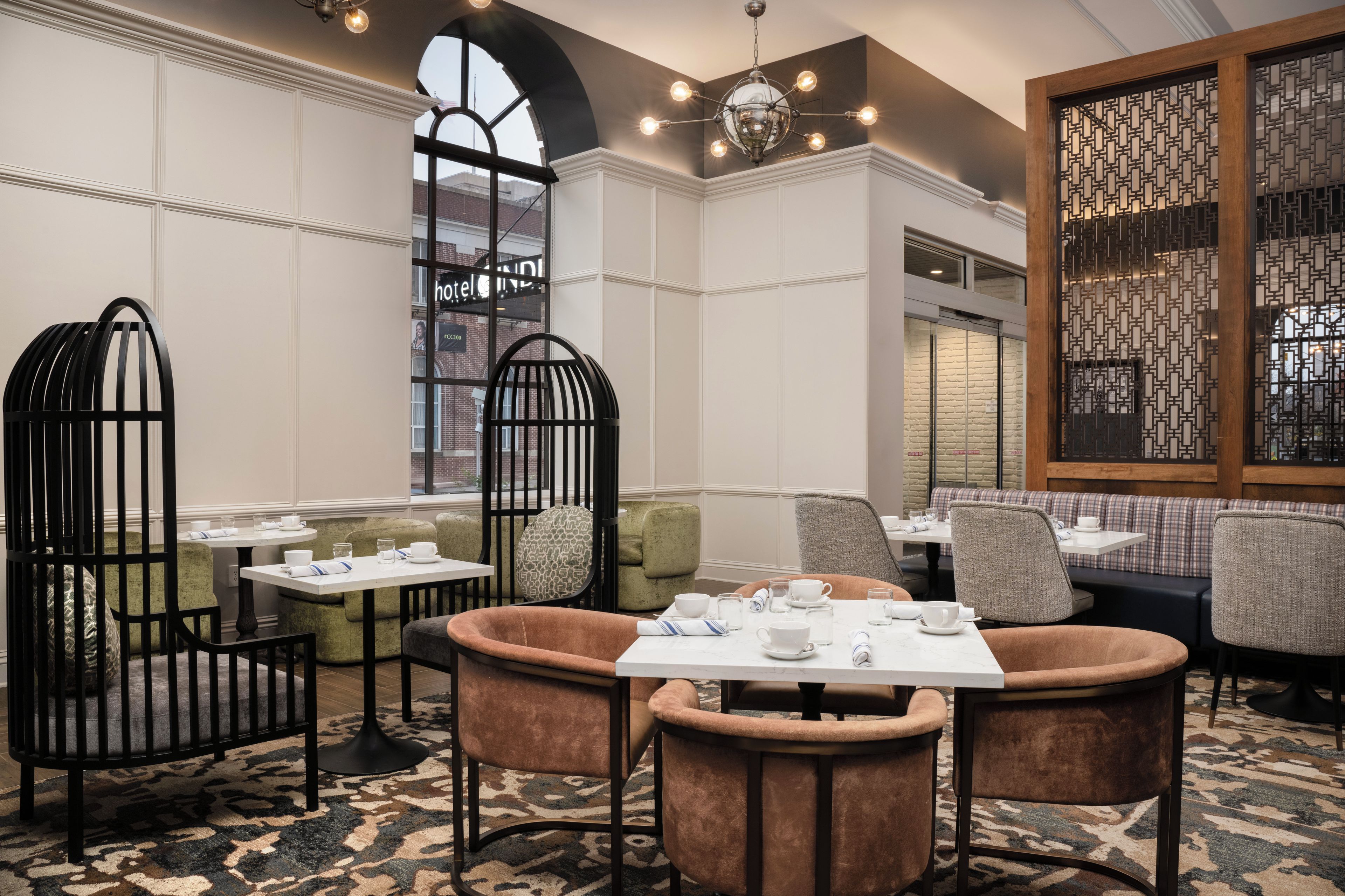 Espaço de refeições de hotel com mesas preparadas para o serviço, assentos acolchoados e uma parede decorativa com padrões geométricos.